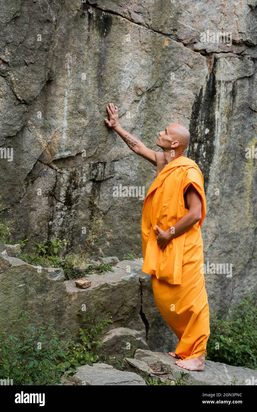 buddhist monk in traditional orange robe touching rock Stock Photo - Alamy