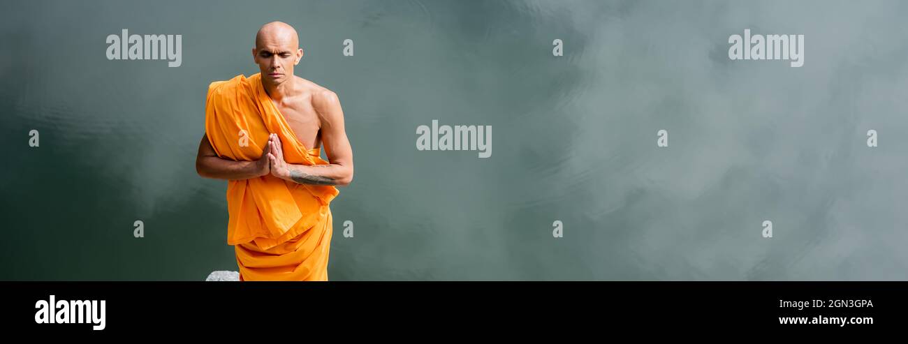 high angle view of buddhist monk in orange robe meditating over river ...