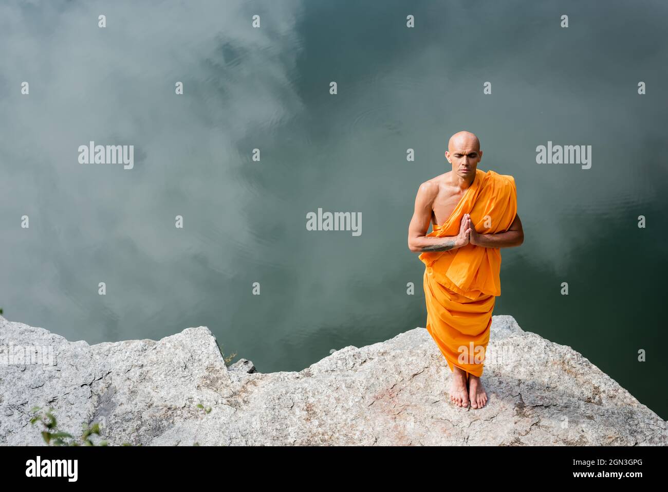high angle view of buddhist in orange robe praying on rocky cliff over ...