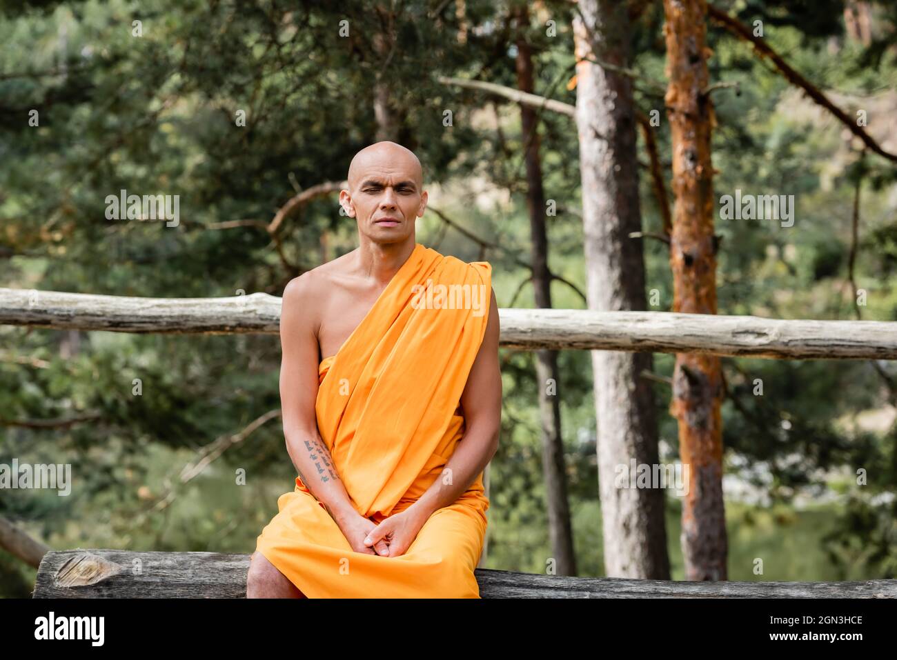 buddhist sitting on log bench and meditating with closed eyes in forest ...