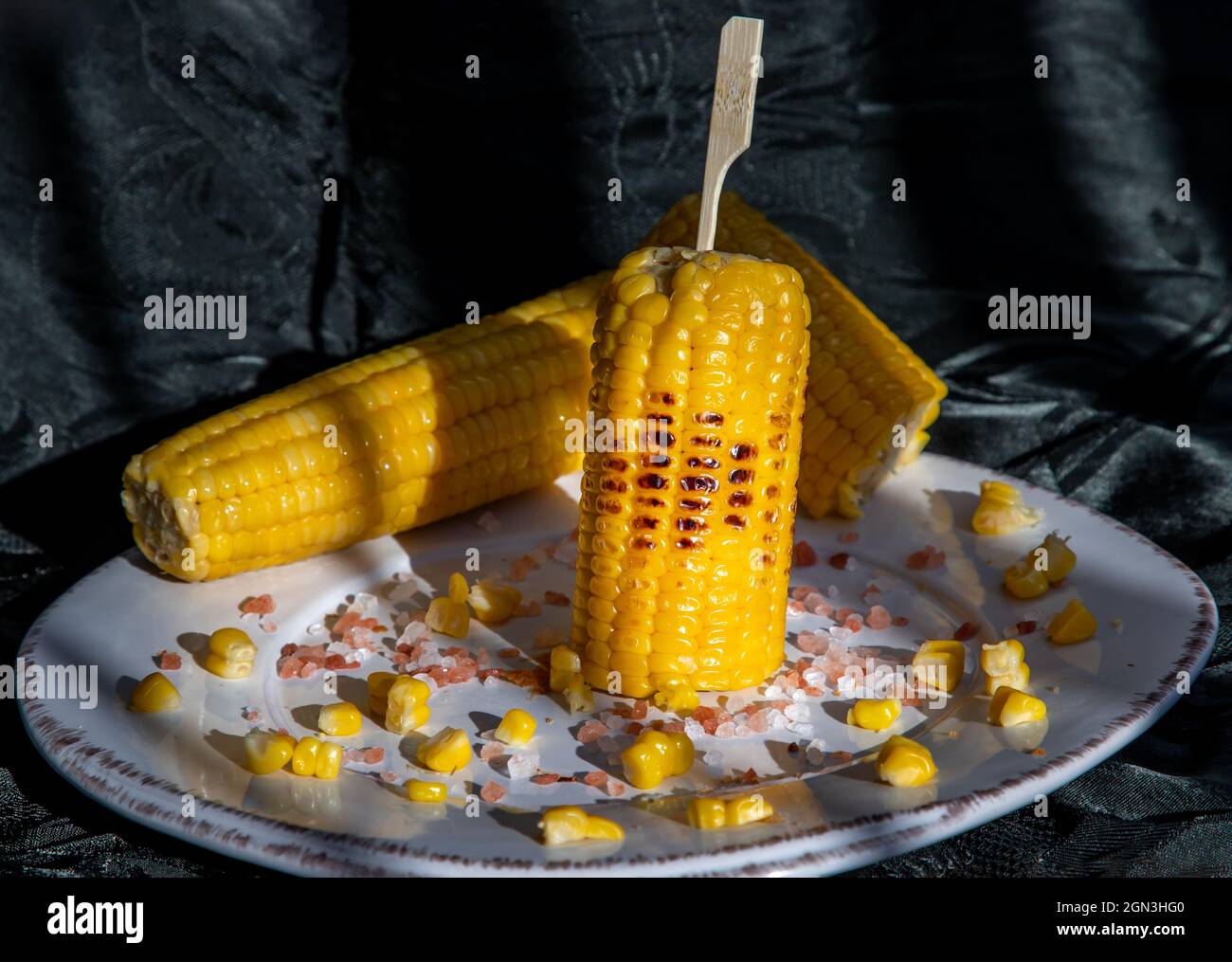 Grilled corn on the cob on classic white plate over dark background ...