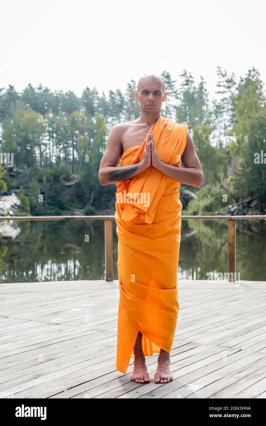 full length view of buddhist monk meditating with praying hands on ...