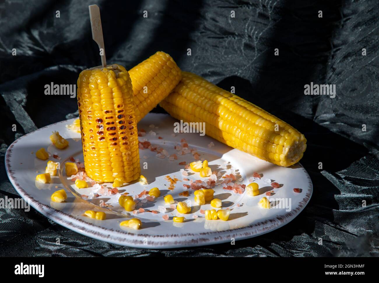 Grilled corn on the cob on classic white plate over dark background ...
