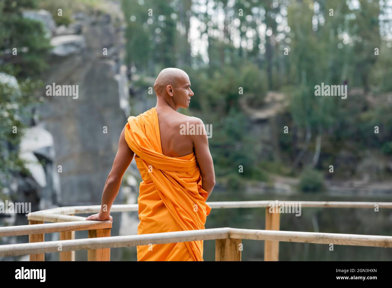 back view of buddhist standing near wooden fence in forest and looking ...