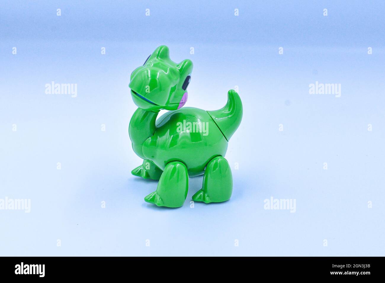 Closeup of the small green toy dinosaur isolated on light bluish ...