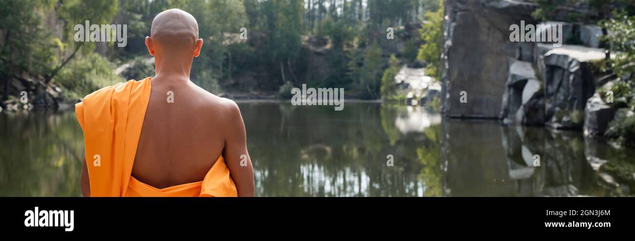 back view of buddhist monk meditating near forest pond, banner Stock ...