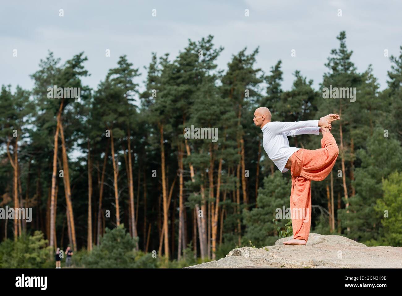 side view of buddhist practicing standing bow pose on rocky cliff in ...