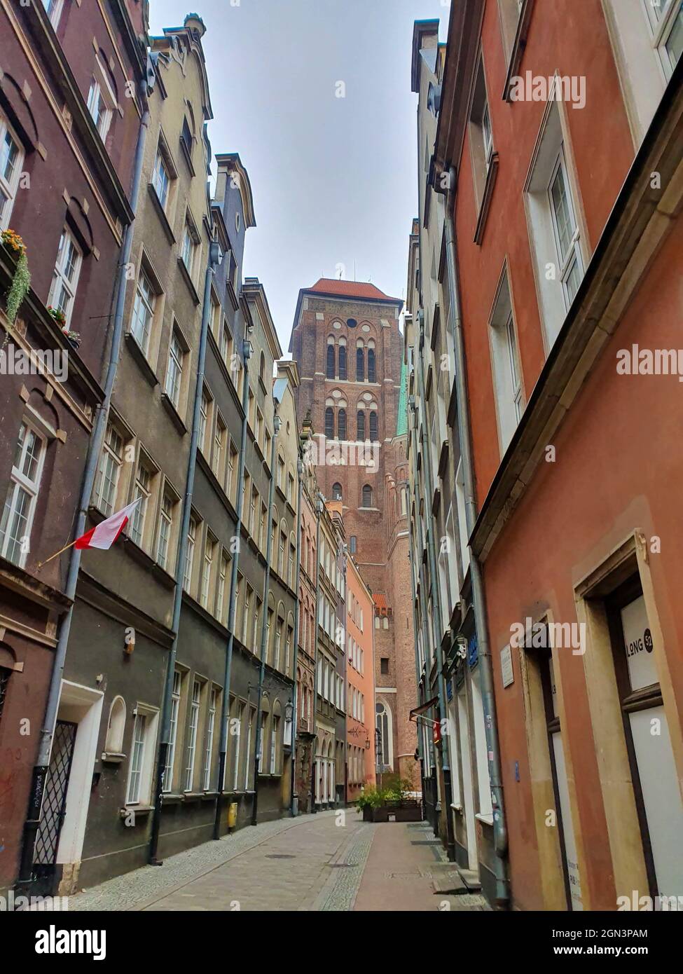 A narrow polish street in the Town of Gdansk overlooked by the tower of ...