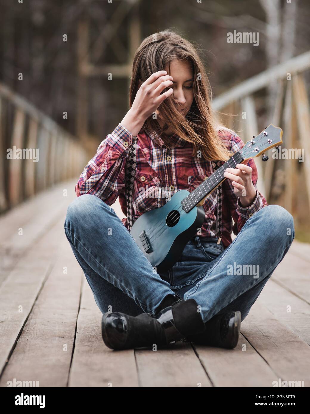 Young Woman Sitting And Playing Ukulele Guitar On Bridge In Autumn