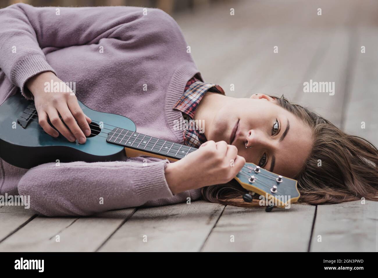 Portrait of young relaxing whith ukulele guitar on bridge in autumn ...