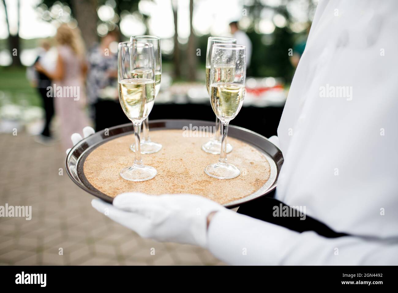 Handsome young butler holding silver tray with two glasses of champagne ...