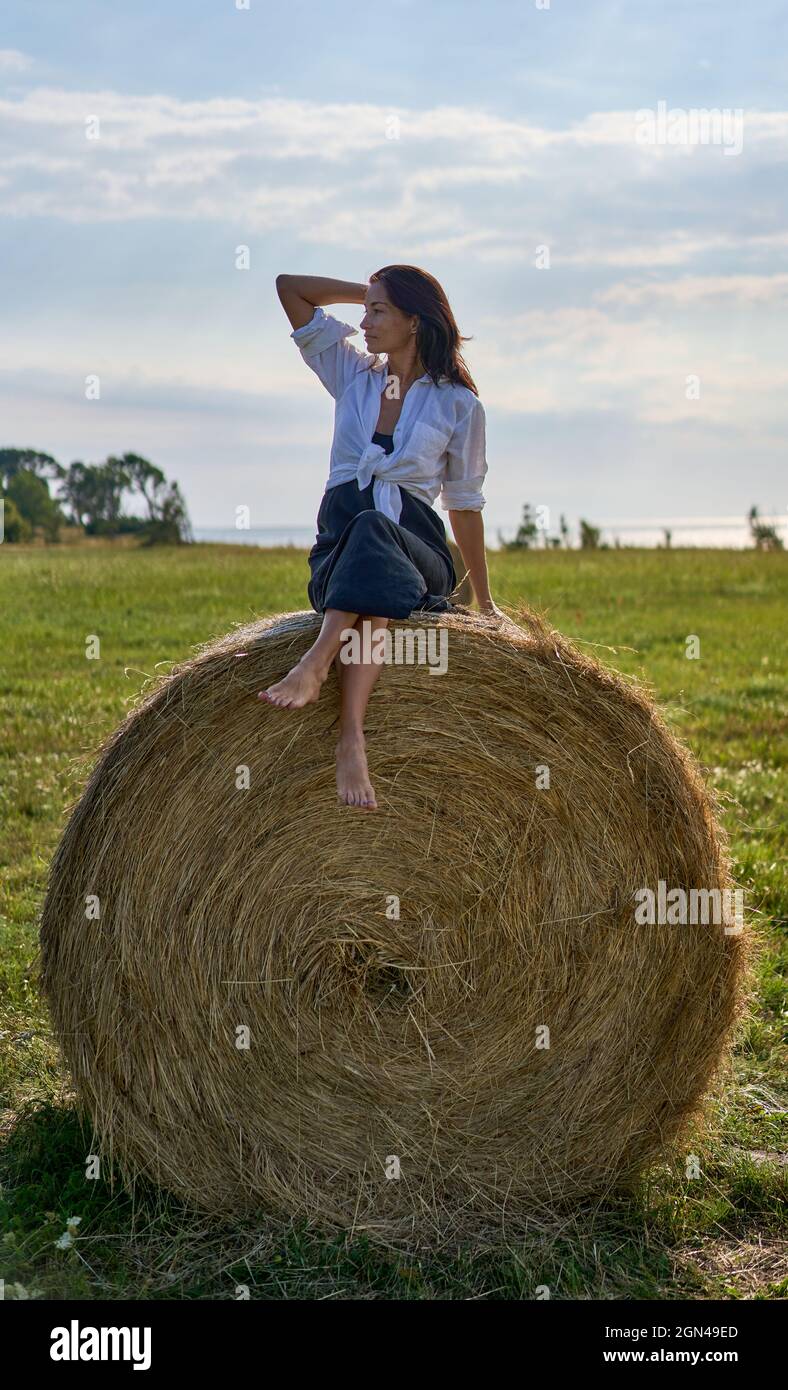 A beautiful young girl sitting on a haystack on a green field Stock ...