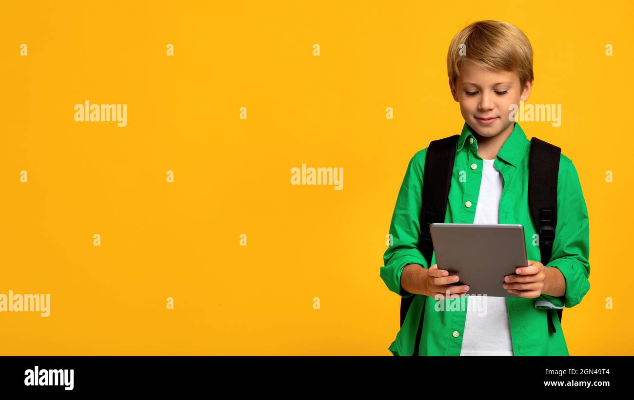 Smiling caucasian teen boy student with backpack typing on tablet and ...