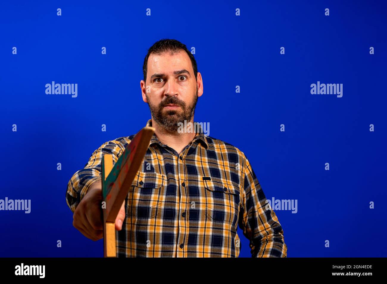 Man in a yellow plaid shirt scratching his back with a wooden sword ...