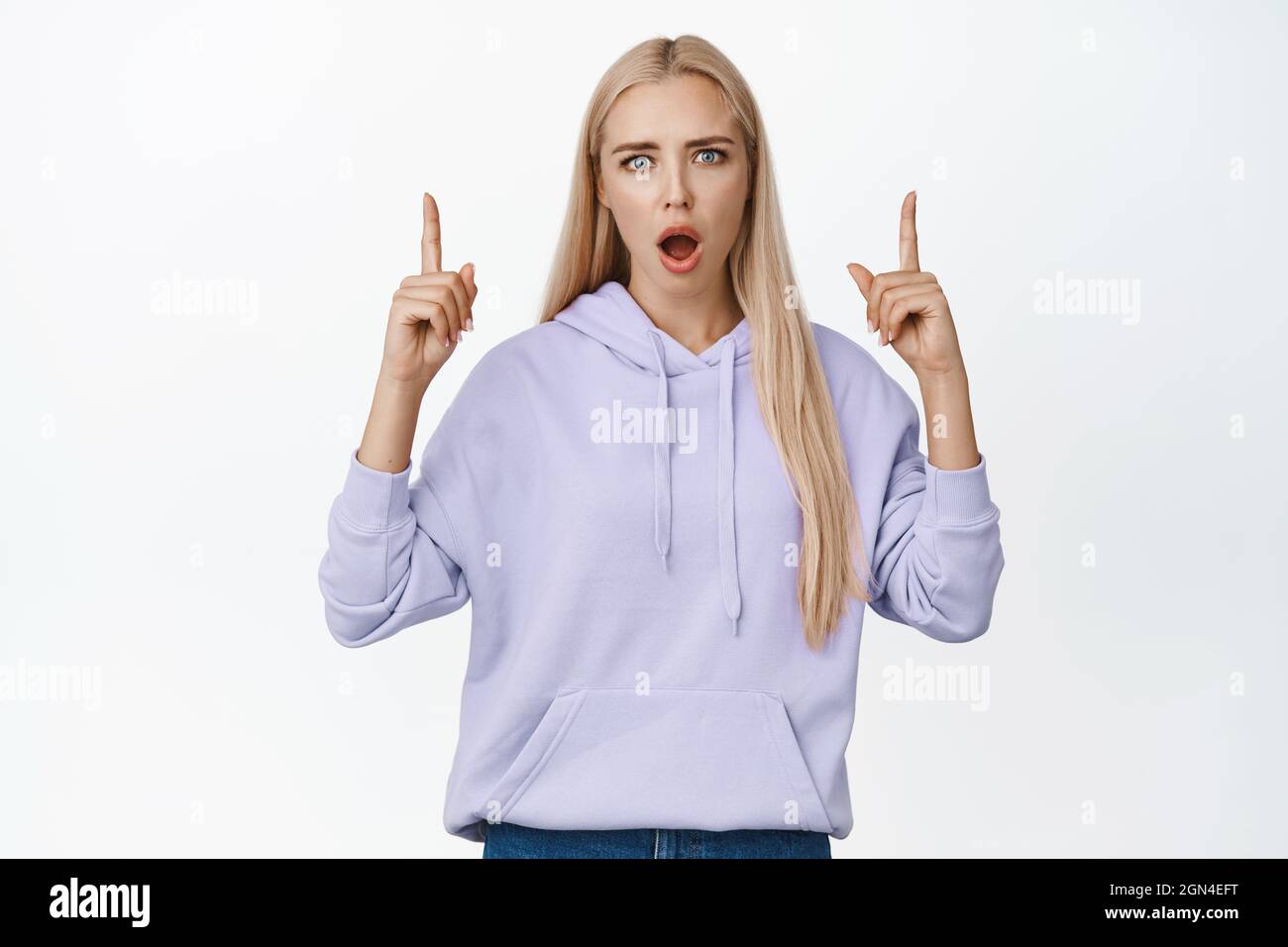 Shocked young woman drop jaw from announcement, pointing fingers up and ...