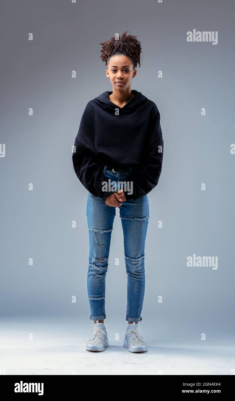 Trendy young Black woman in frayed jeans and hoodie standing looking ...