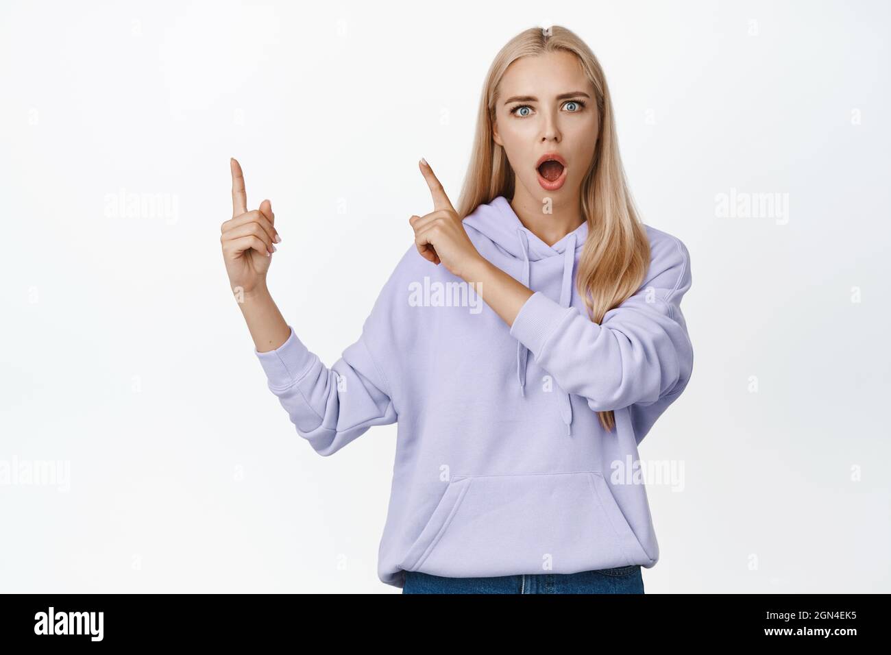 Shocked blond girl pointing fingers at upper left corner, drop jaw and ...
