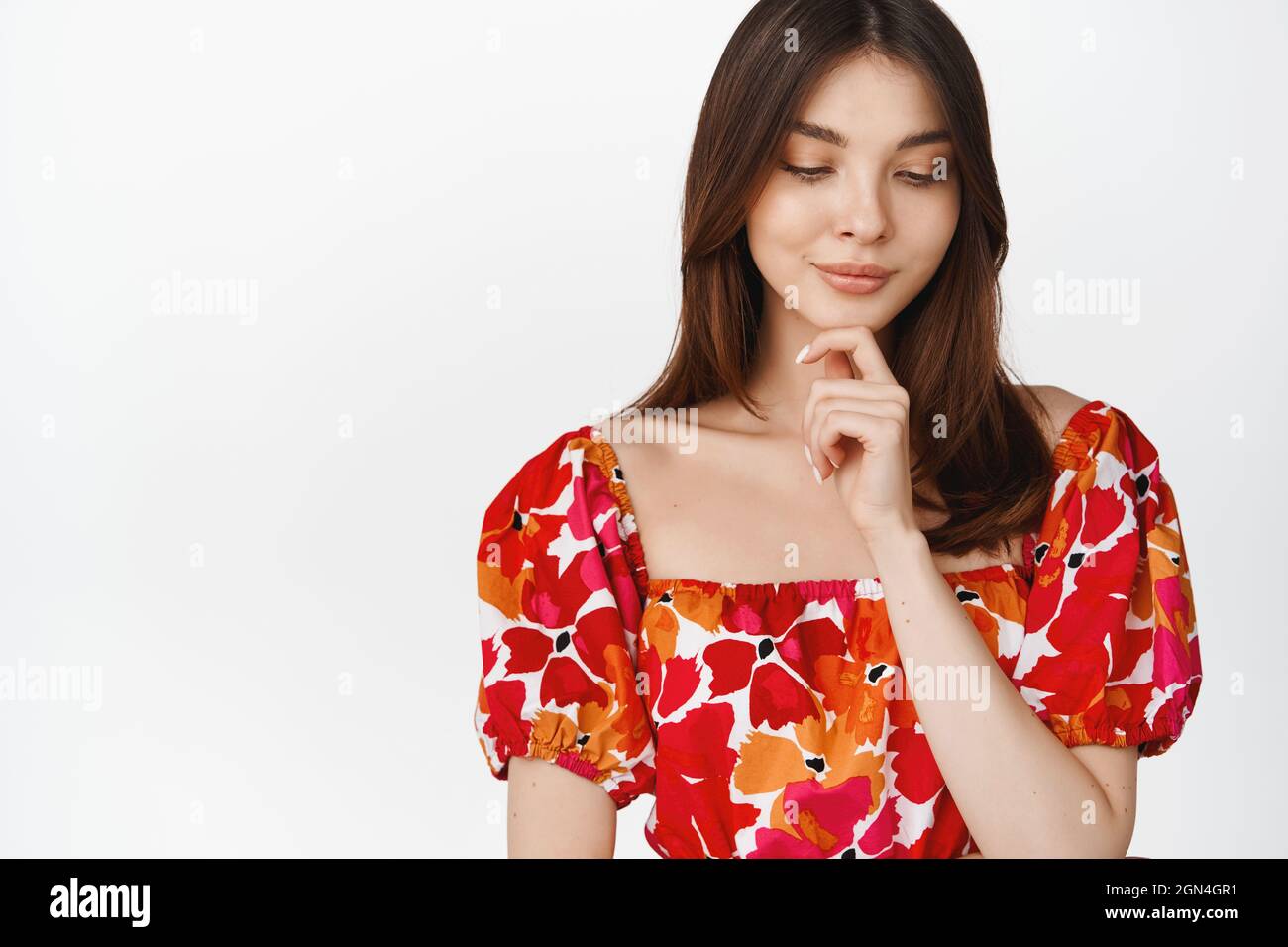 Beautiful, feminine young woman gazing down, touching her face ...
