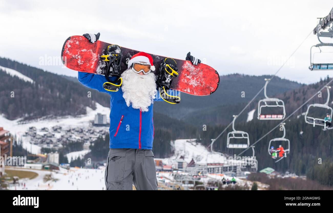 Santa Claus with snowboard against snowy winter mountain ski resort ...