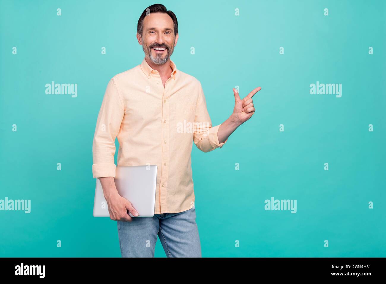 Photo of confident mature man point empty space hold laptop wear peach ...