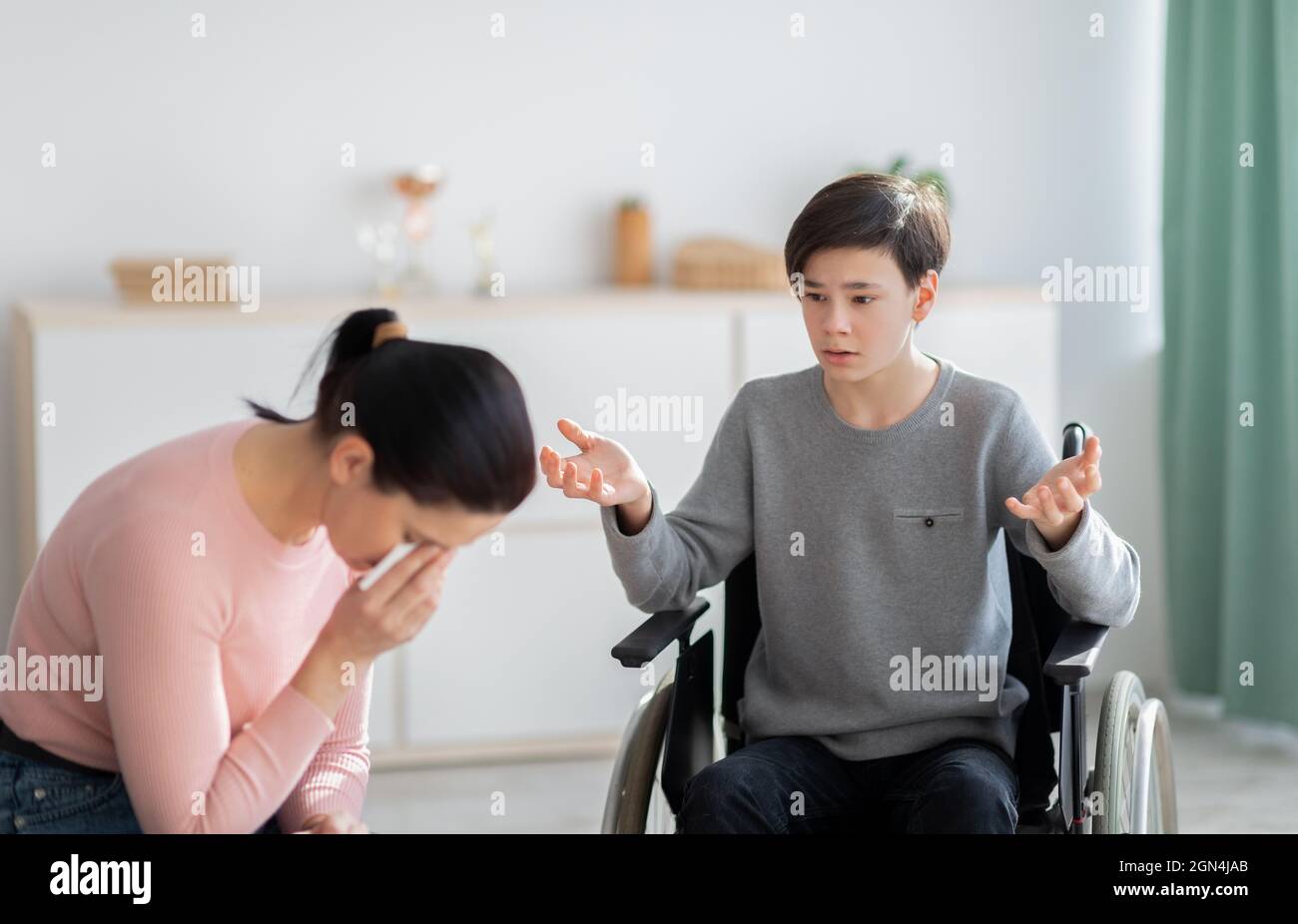 Unhappy mother crying and her disabled teen son in wheelchair trying to ...