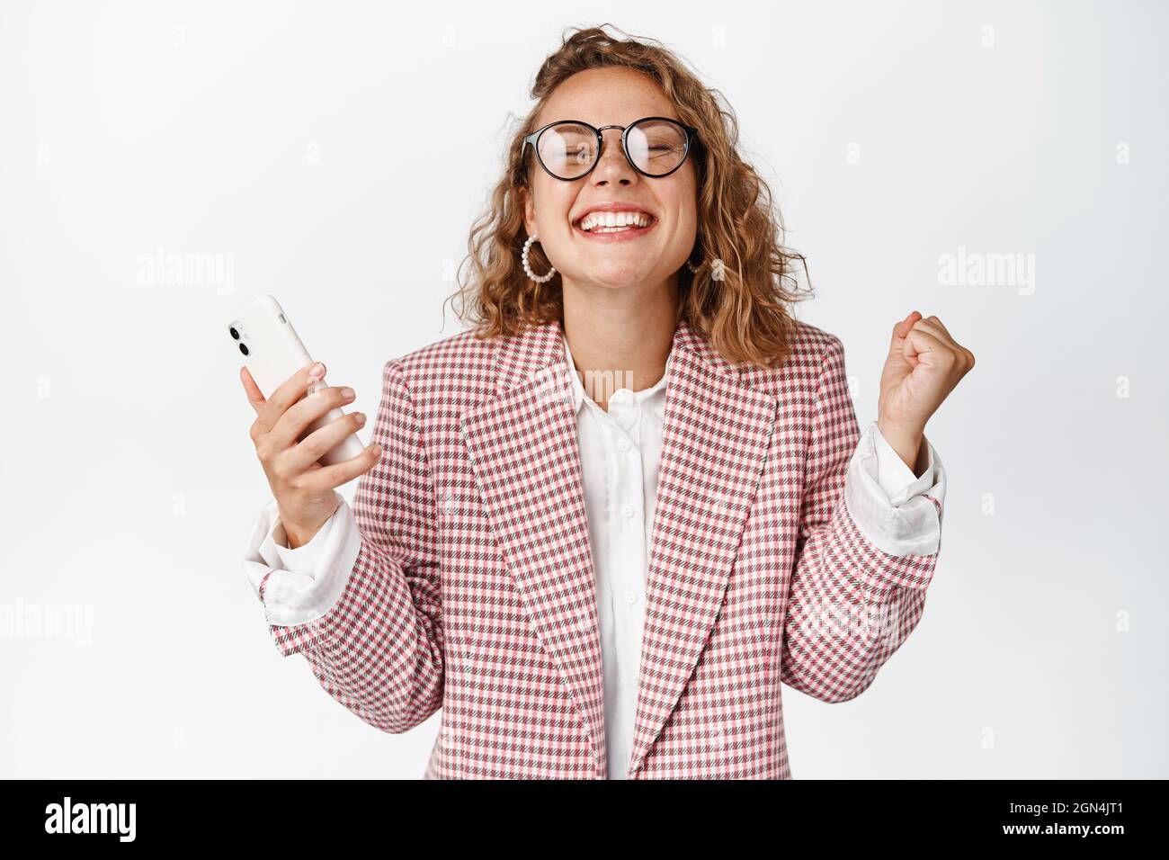 Happy businesswoman in suit celebrating, holding smartphone and ...