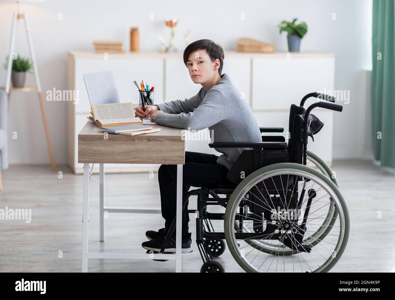 Disabled teenager in wheelchair learning online with books and laptop ...