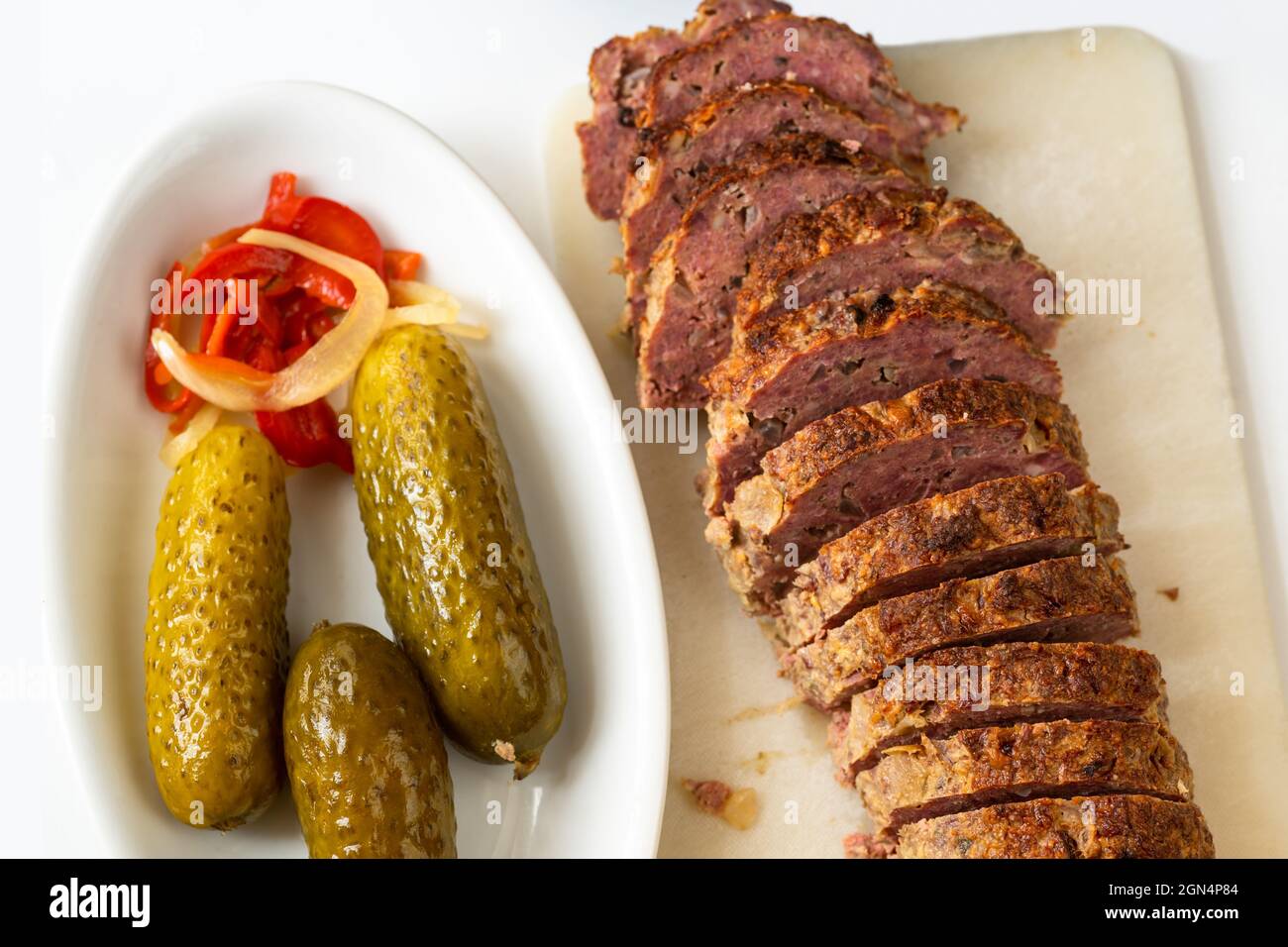 Sliced baked beef meatloaf on kitchen board, pickled cucumber with ...