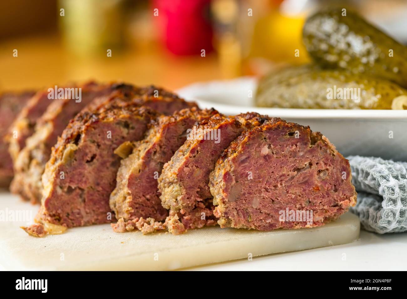 Baked sliced beef meatloaf on kitchen board, pickled cucumber and towel ...