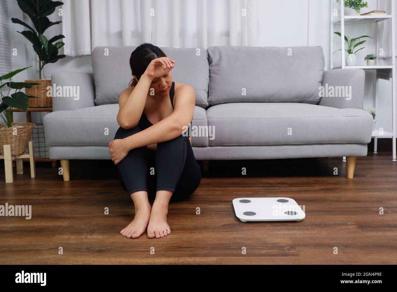 Young Asian woman sitting on the floor looking at the weight scale ...