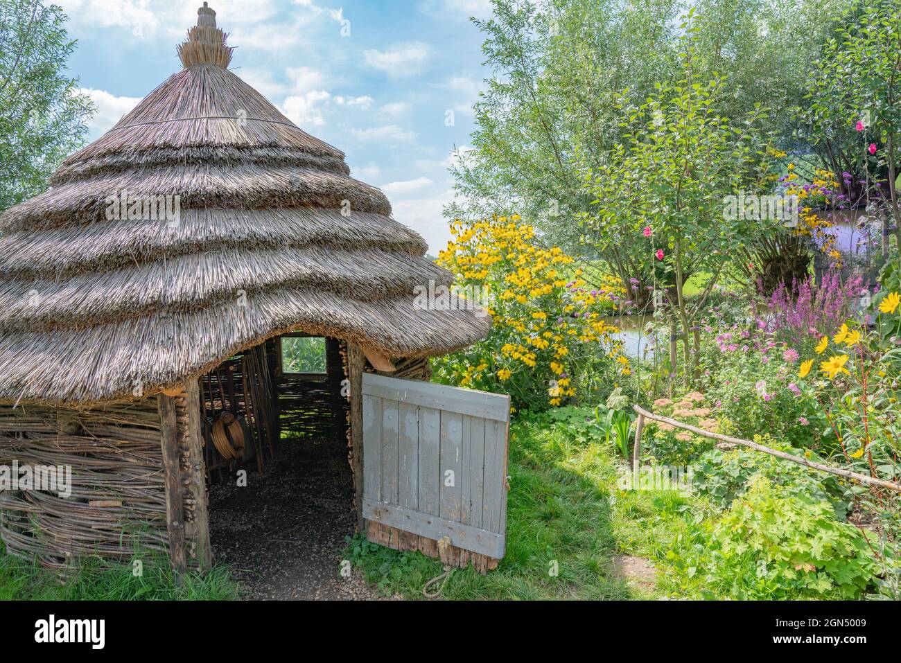 Round cane walled thatched roof hut in garden of wildflowers next to ...