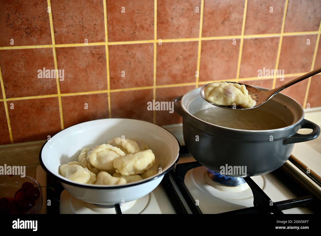 The pastry chef takes out cooked dumplings from boiling water into a ...