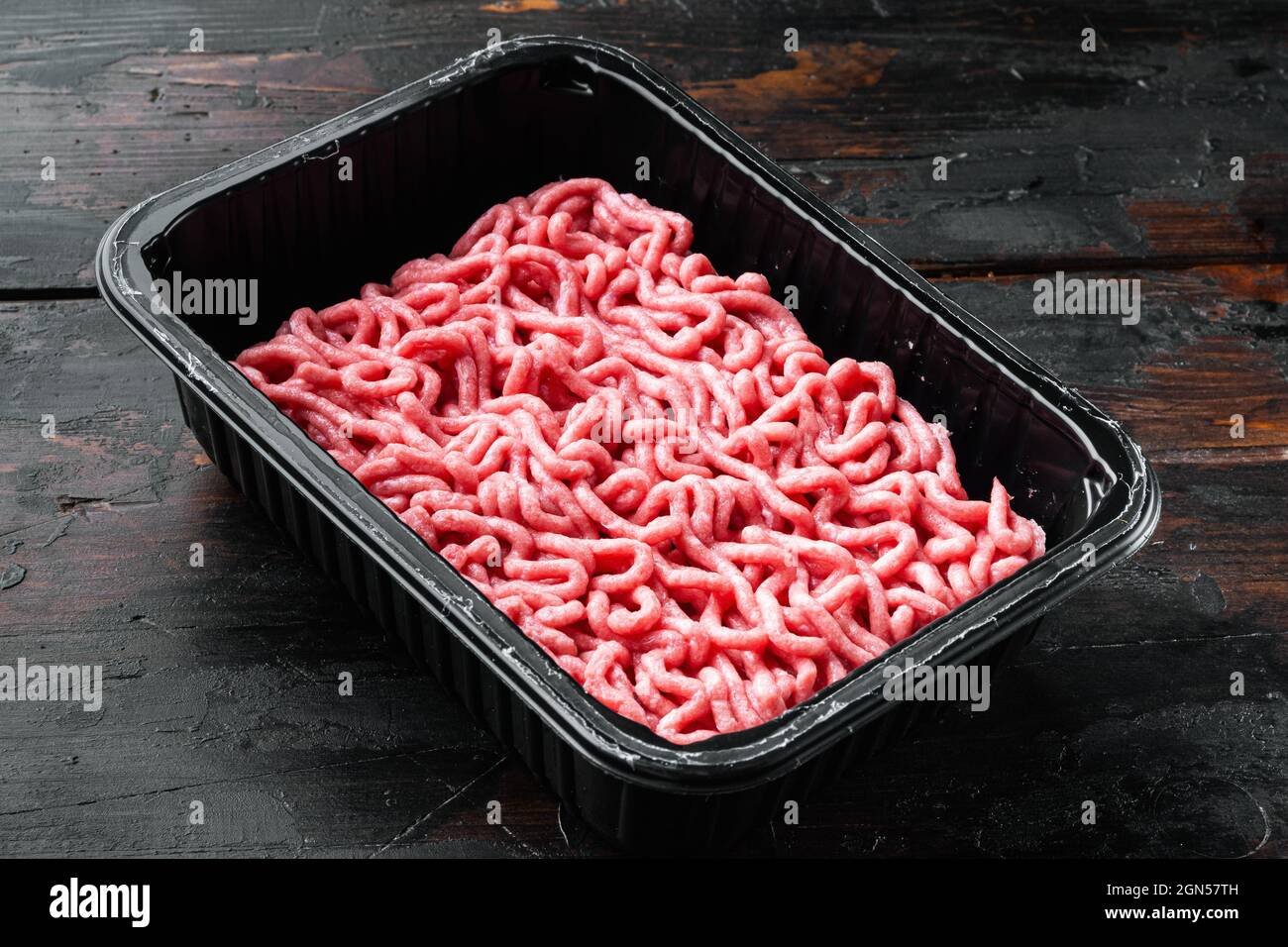 Ground beef meat in plastic tray set, on old dark wooden table ...