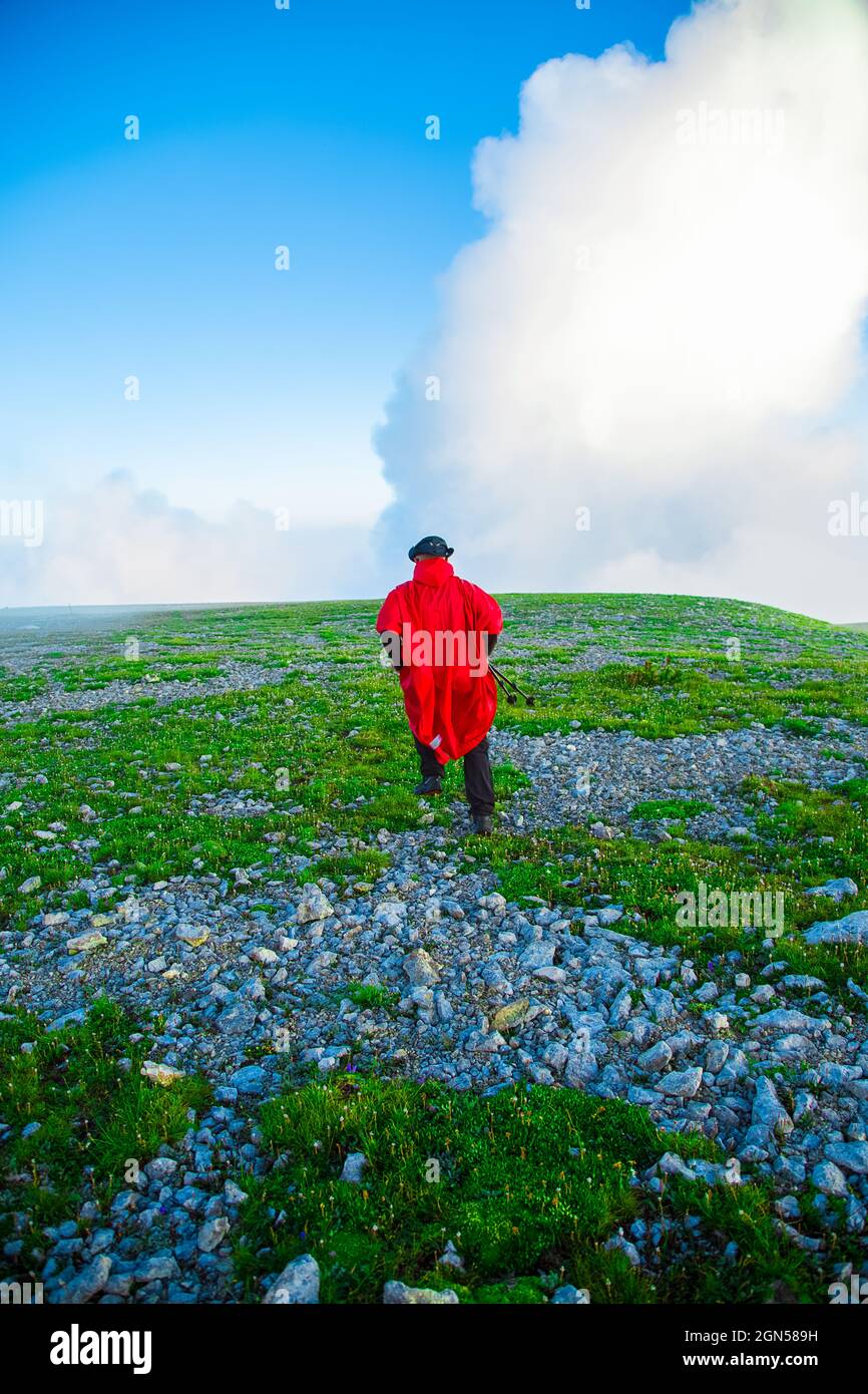 Alpinist in bright red coat in alpine valley. At the top of a mountain ...