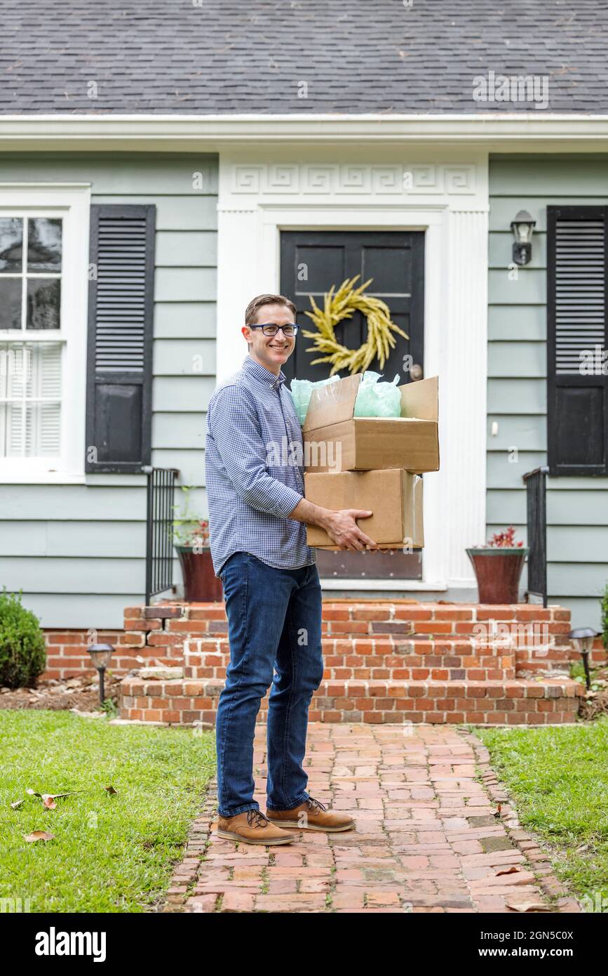 A man and father holding moving boxes outside a small blue cottage ...