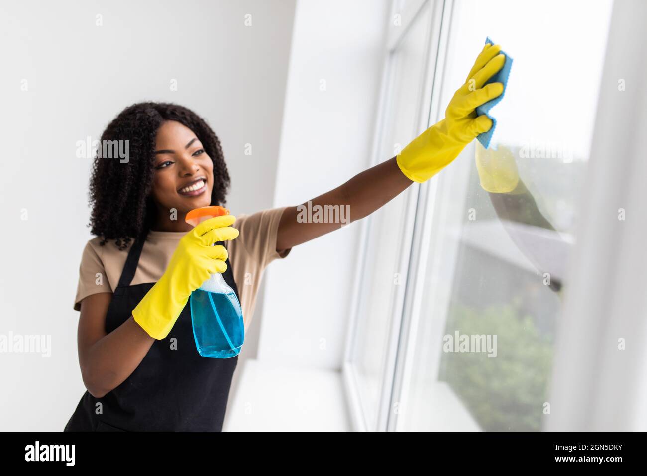 Young african woman in yellow gloves washes the window. House cleaning ...