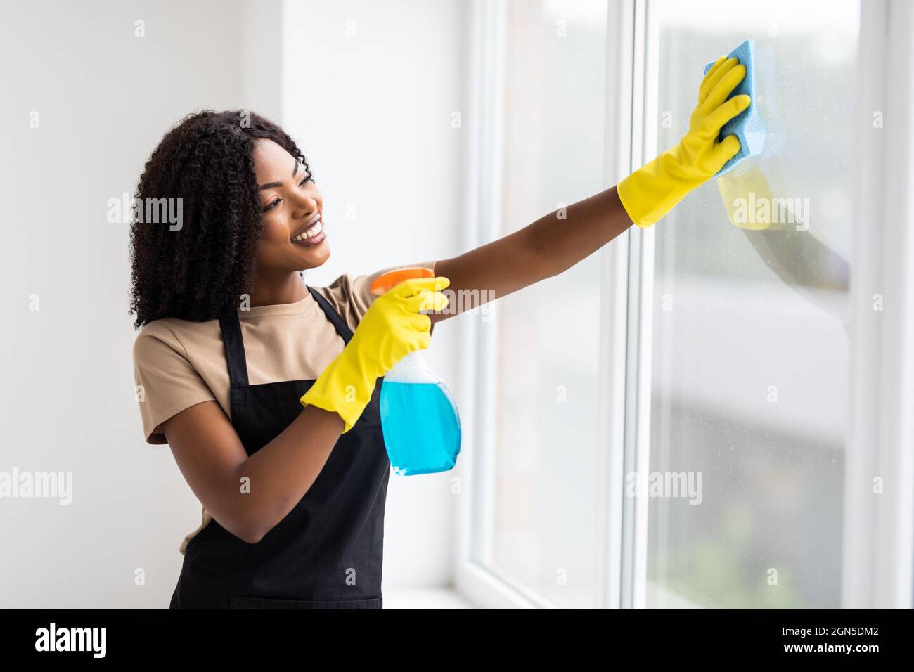 Young african woman in yellow gloves washes the window. House cleaning ...