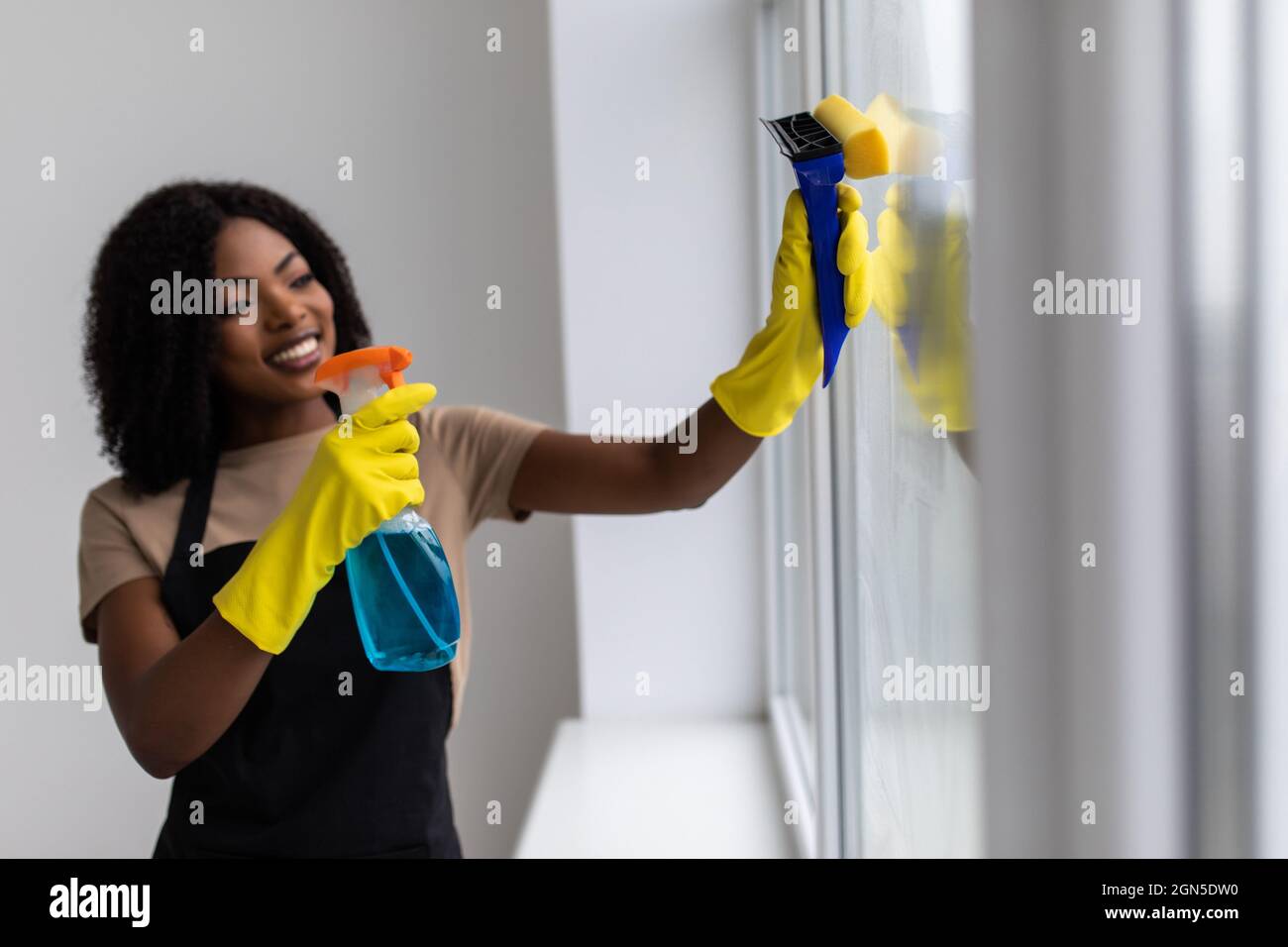 Beautiful african woman is using a duster and a spray, looking at ...