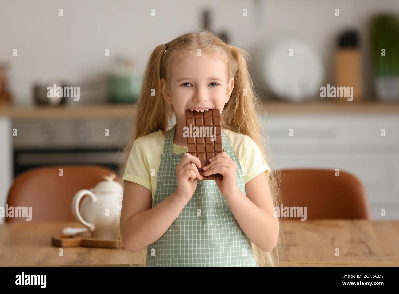 Cute little girl eating sweet chocolate in kitchen Stock Photo - Alamy