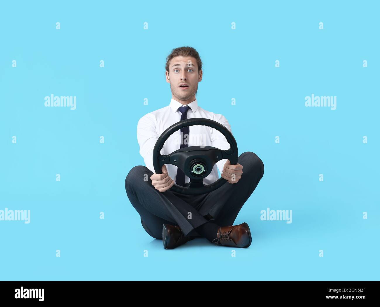 Shocked young man with steering wheel on color background Stock Photo ...