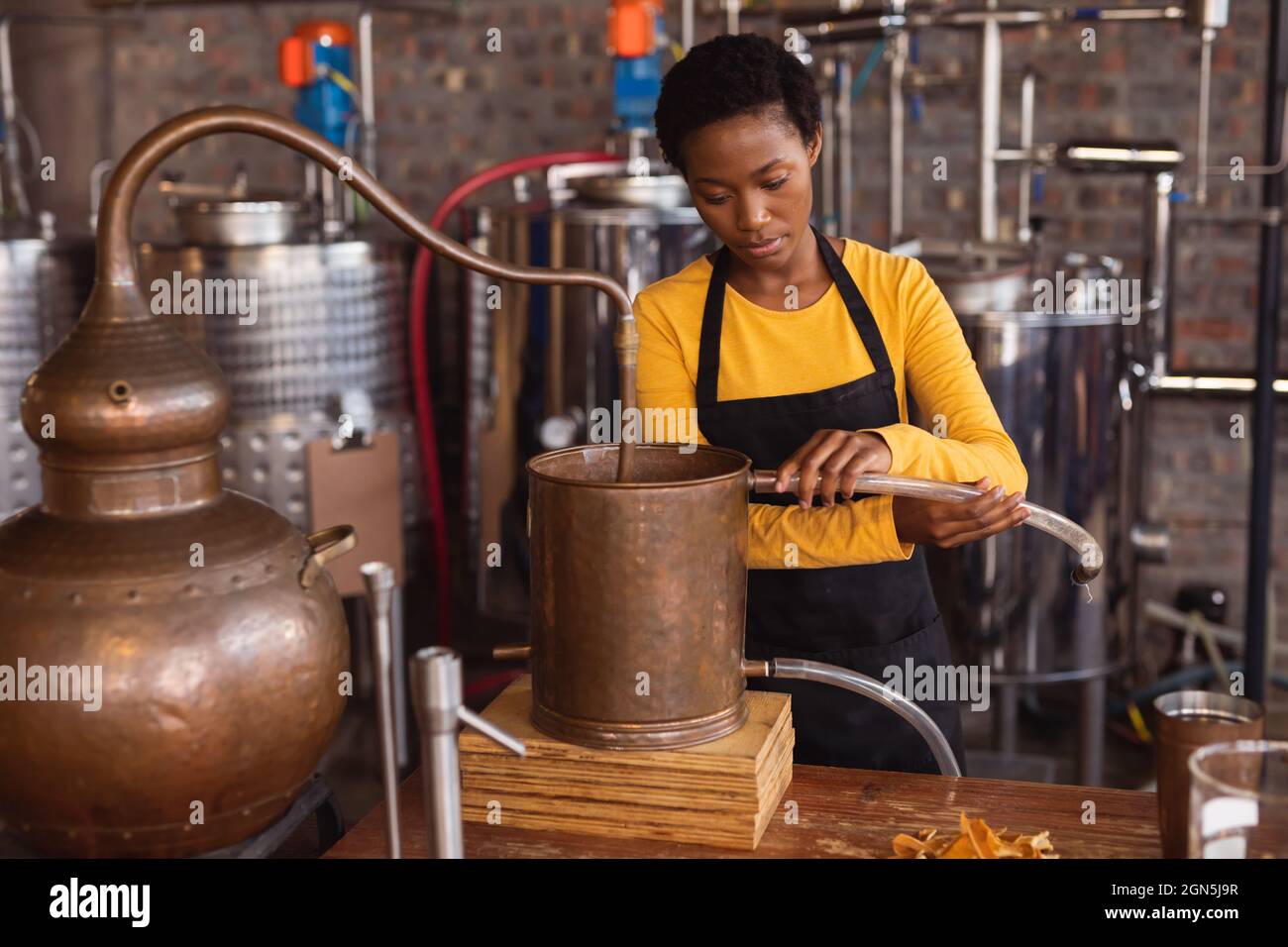 African american woman connecting pipe to distillation equipment at gin ...