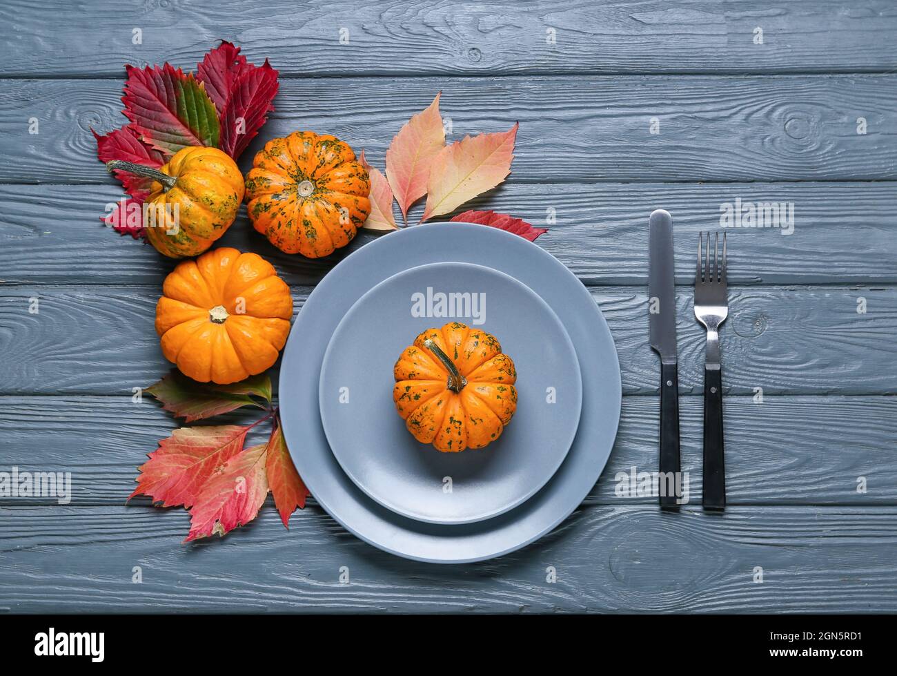 Beautiful table setting with pumpkins and autumn leaves on color wooden ...