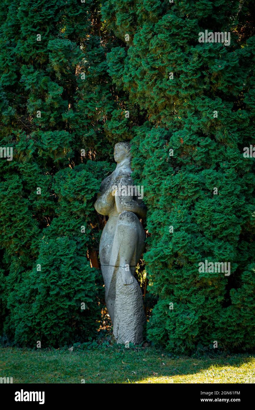 Statue of a woman hidden between green trees in the park Stock Photo ...