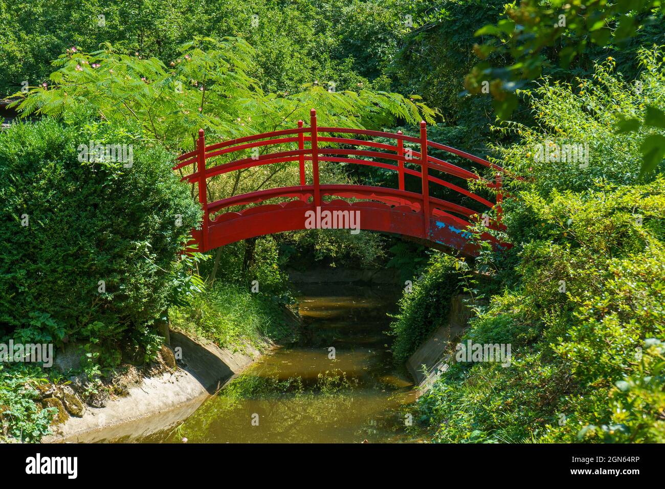 Small weathered red-painted metal bridge over the creek surrounded by ...