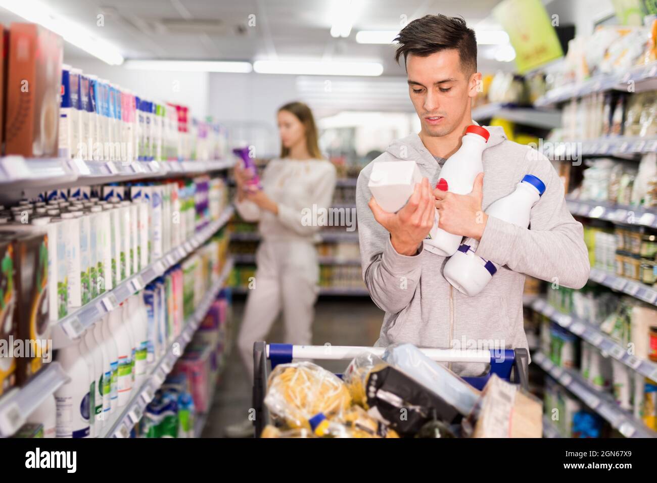Young smiling male customer choosing milk and dairy products in ...