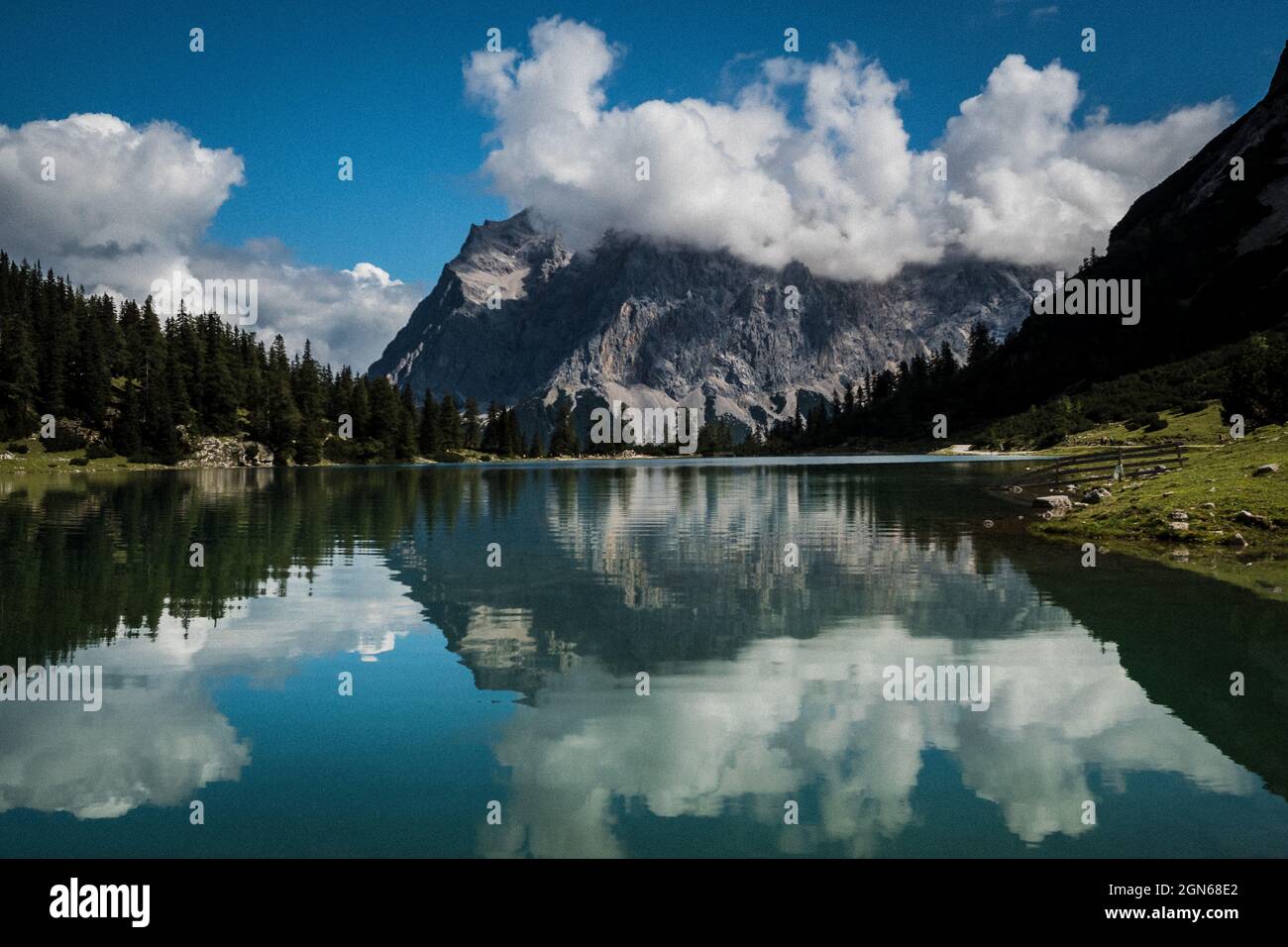Scenic view of a calm lake with reflection of trees and cloudy sky in ...