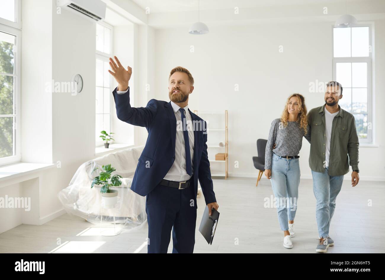 Real estate agent giving happy young customers a tour about a new ...