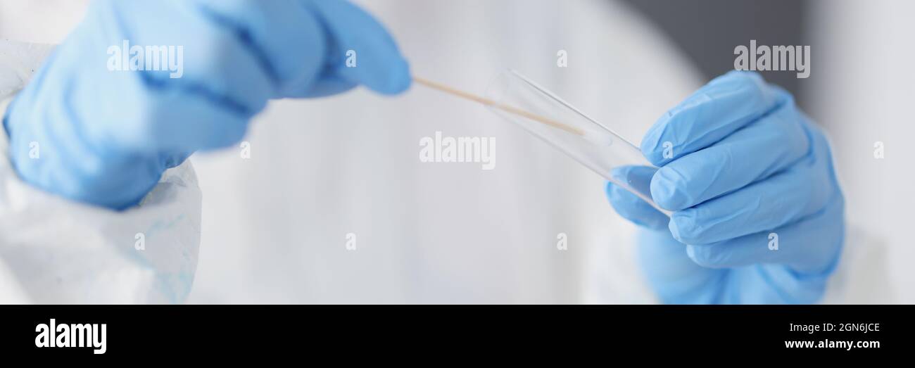 Researcher in protective suit and gloves holds test tube with smear of ...