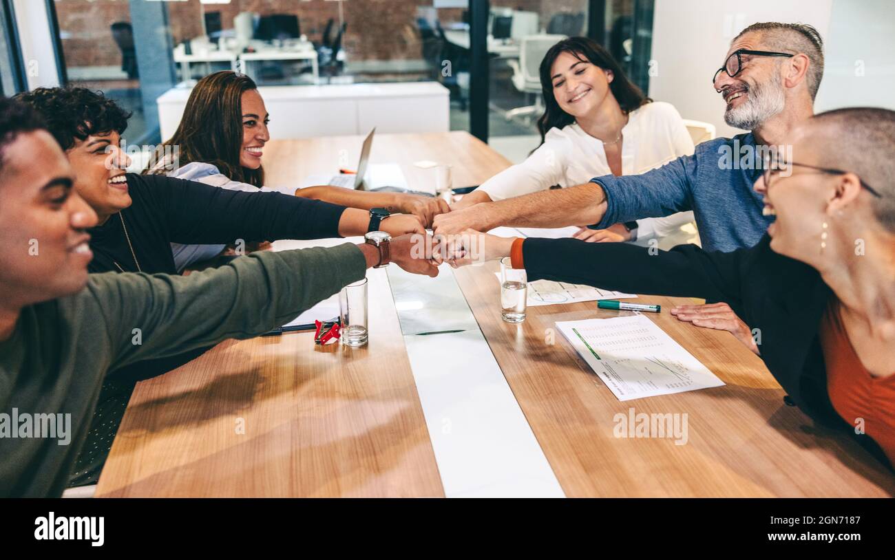 Cheerful group of businesspeople bringing their fists together while ...