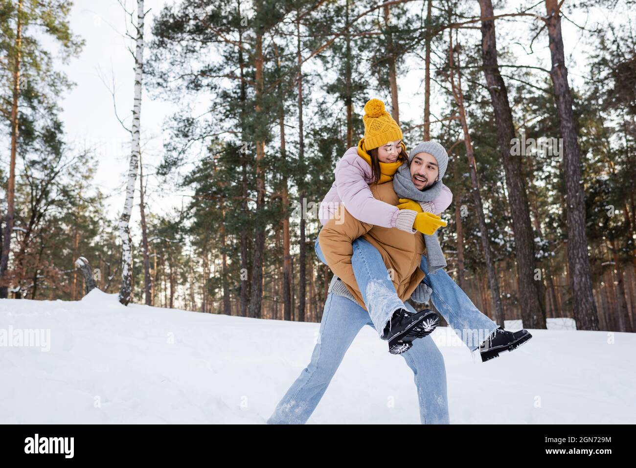 Happy woman piggybacking on boyfriend while having fun in winter park ...